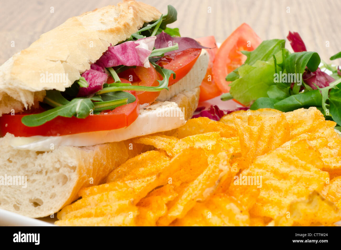 Baguette filled with Brie cheese served with salad and flavoured chips ...