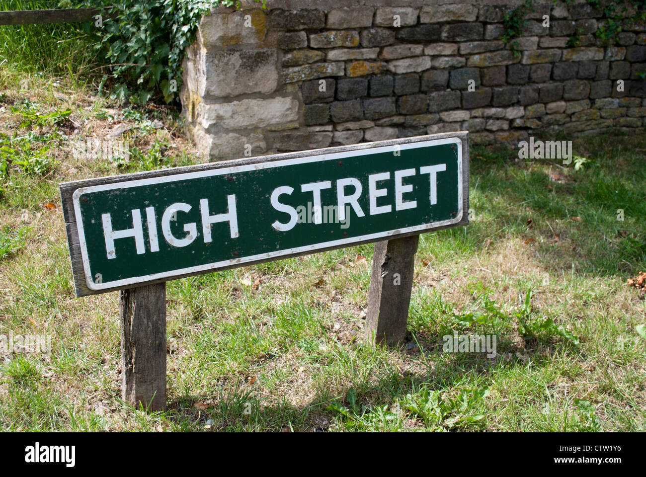 'High Street' sign on two posts on grass with stone wall behind Stock ...