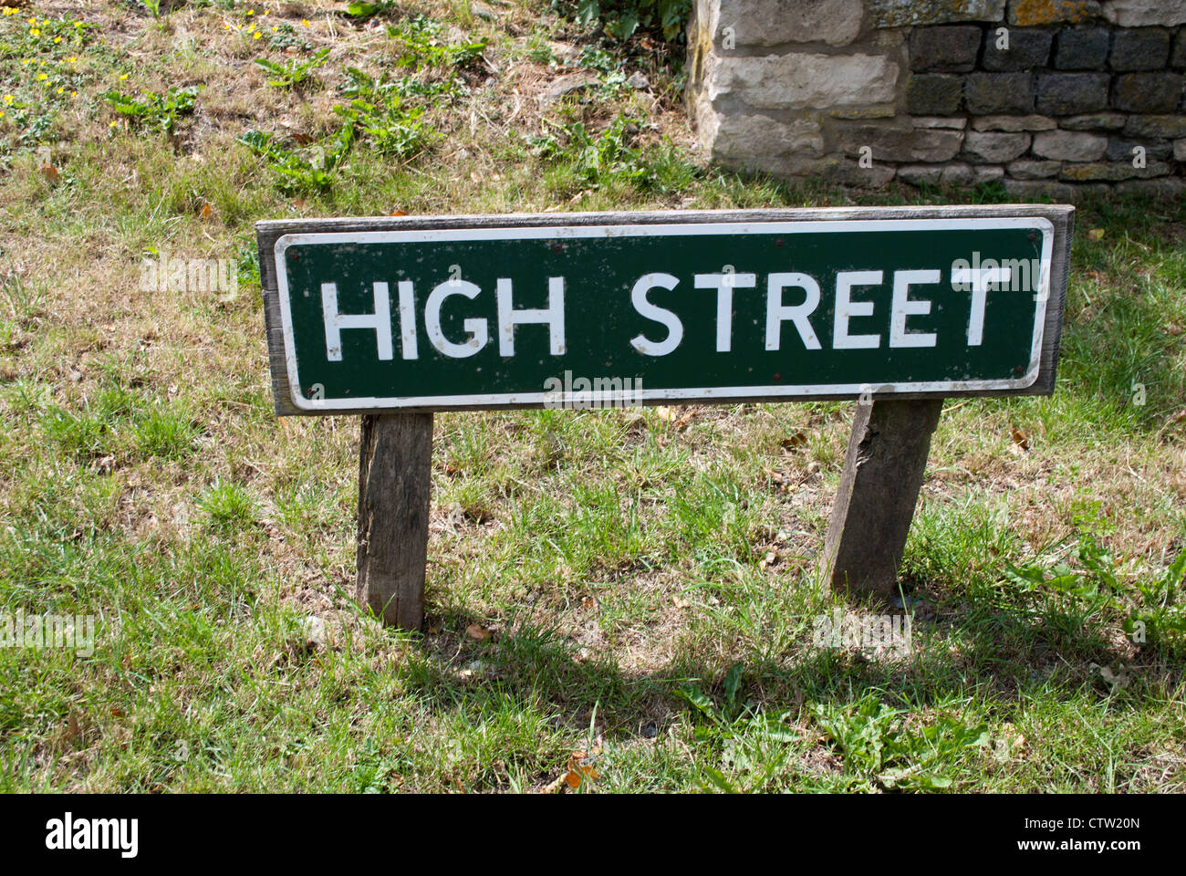 'High Street' sign on two posts on grass with stone wall behind Stock ...