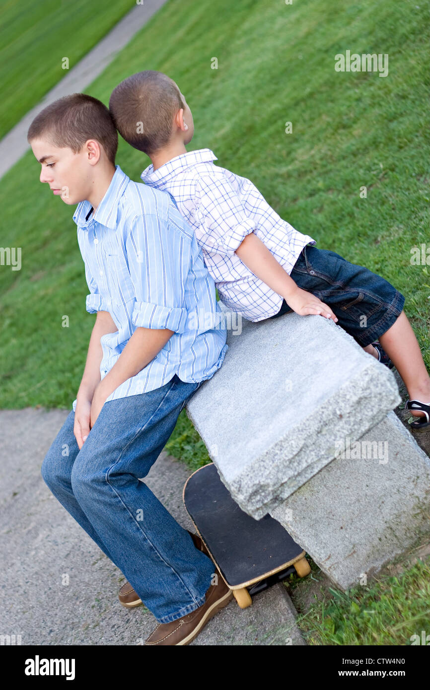 Two brothers sitting back to back on a bench in the park looking very ...