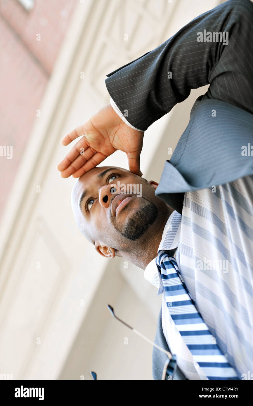 A young business man holds his hand to his forehead as he looks off at ...
