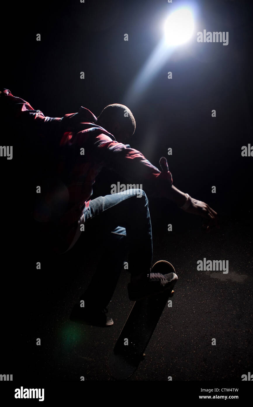 A skateboarder performs tricks under dramatic rim lighting with lens ...