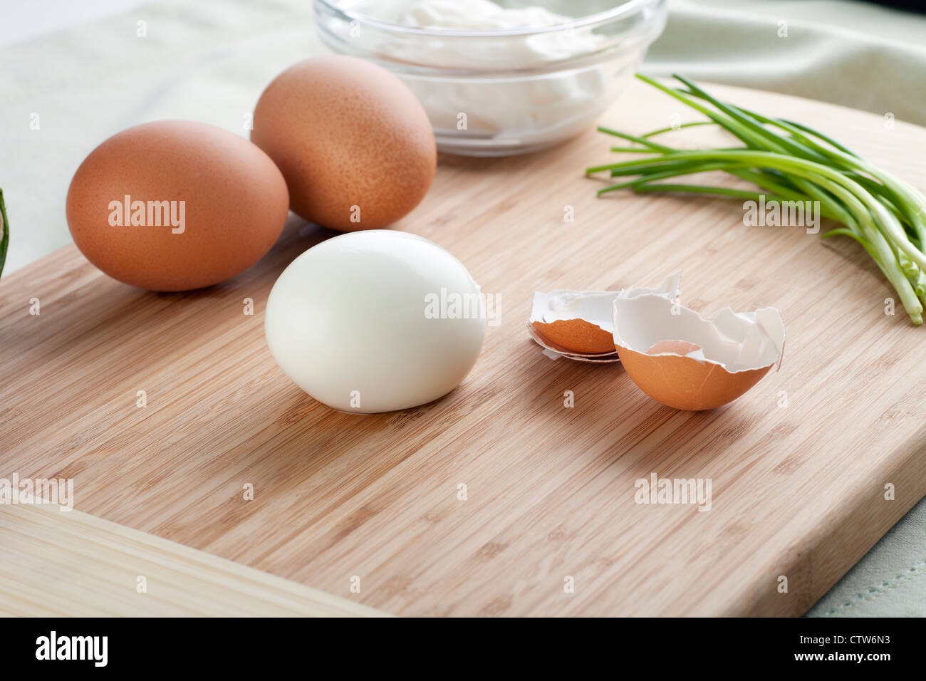 Peeled hard boiled egg with shells, two whole eggs and chives on ...