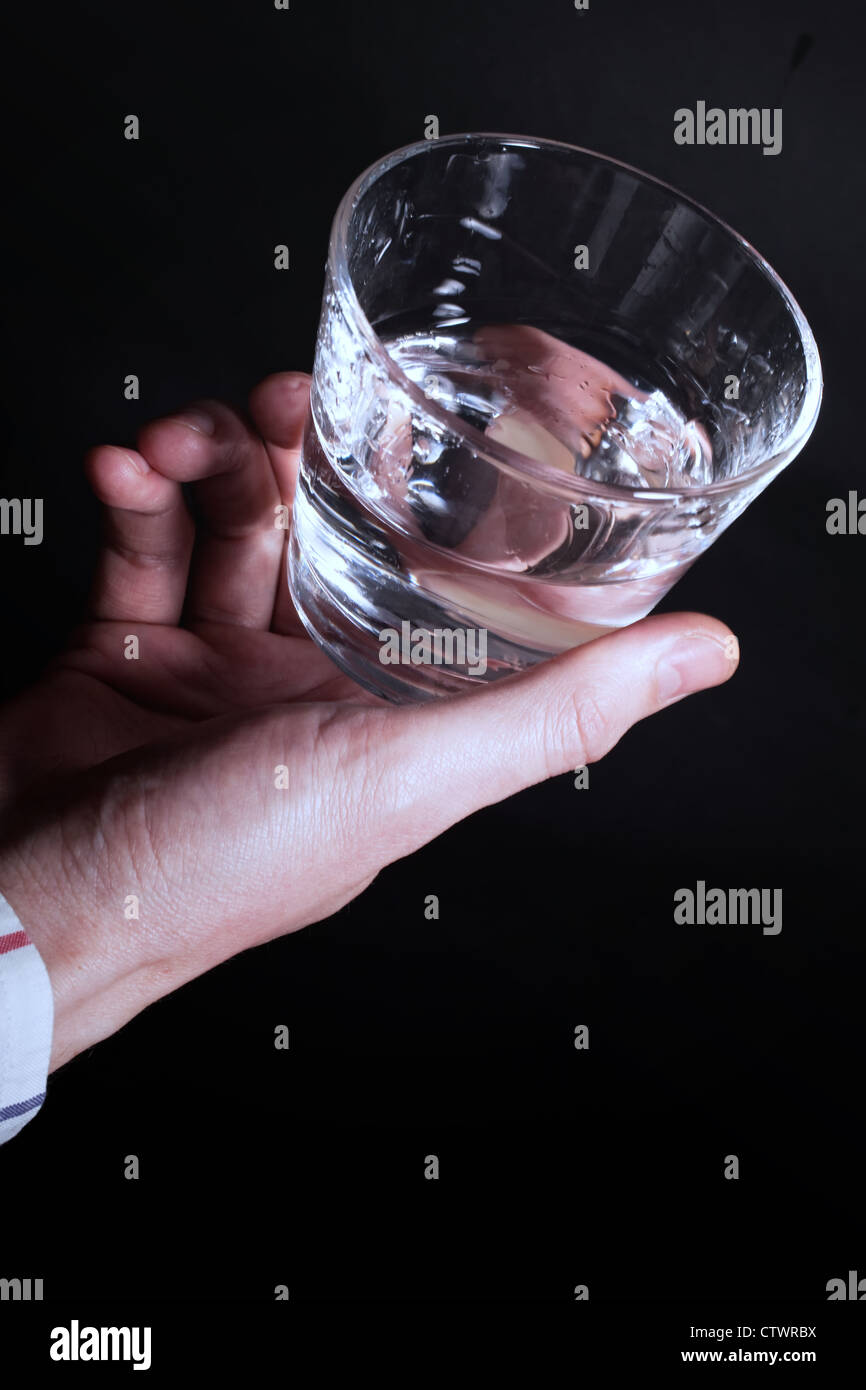 A hand holding a clear glass of water on a black background close up ...