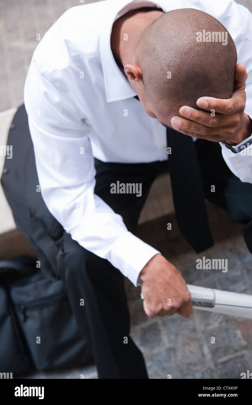 Frustrated businessman holding a rolled up newspaper, head in hand ...