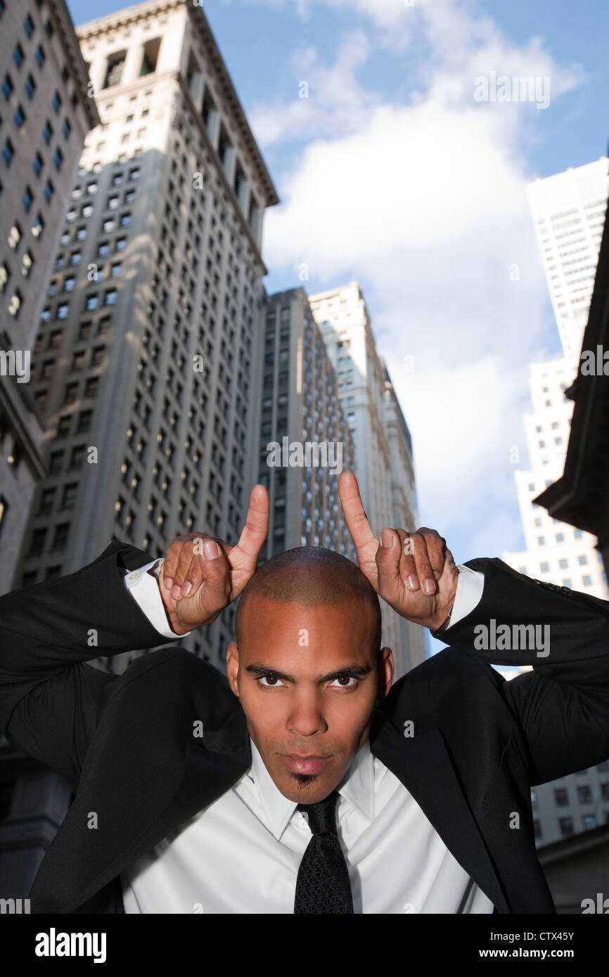 Portrait of a serious businessman gesturing horn sign on head in front ...