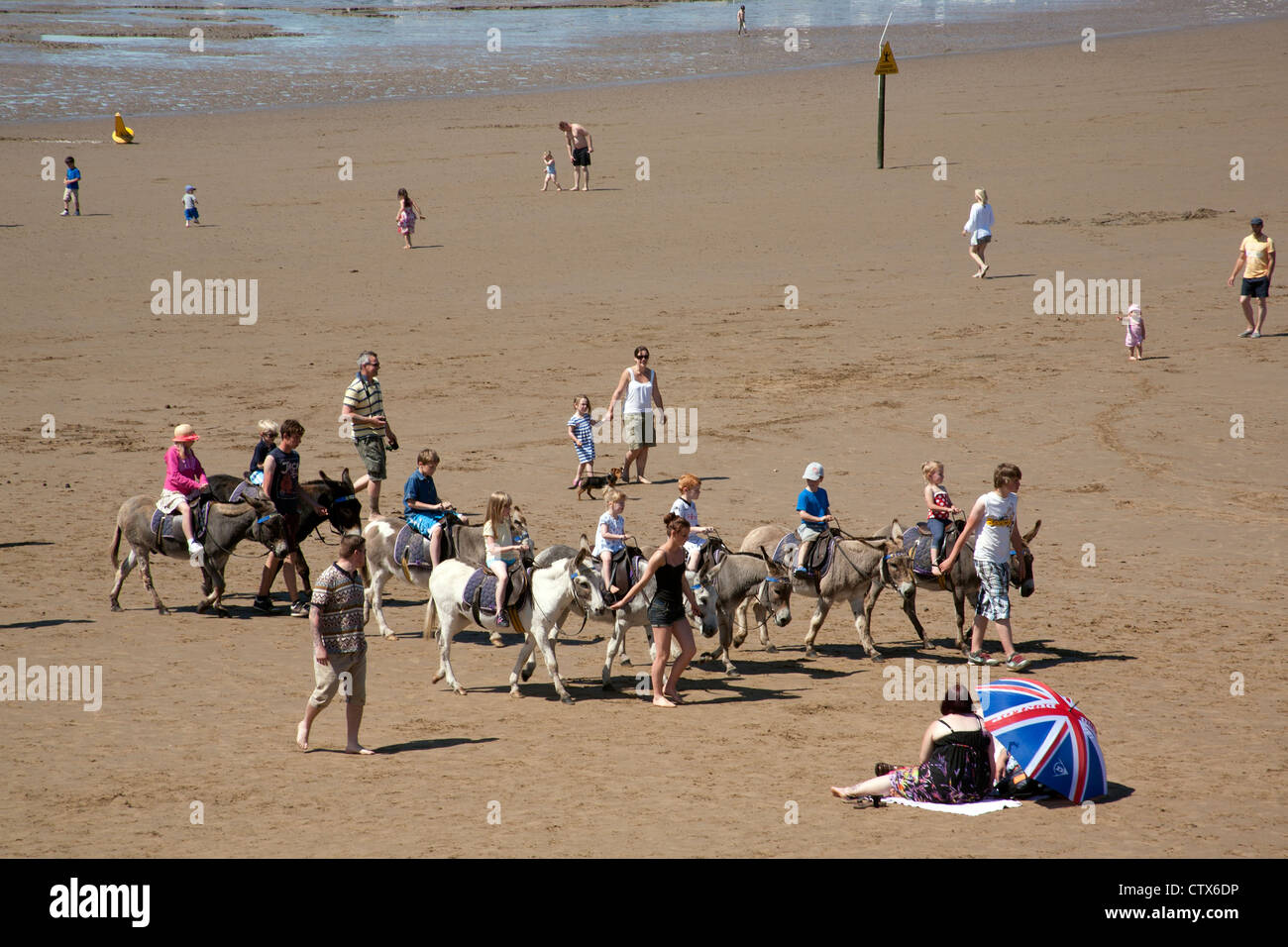 Donkey rides on the beach going past a lady with a union flag umbrella ...