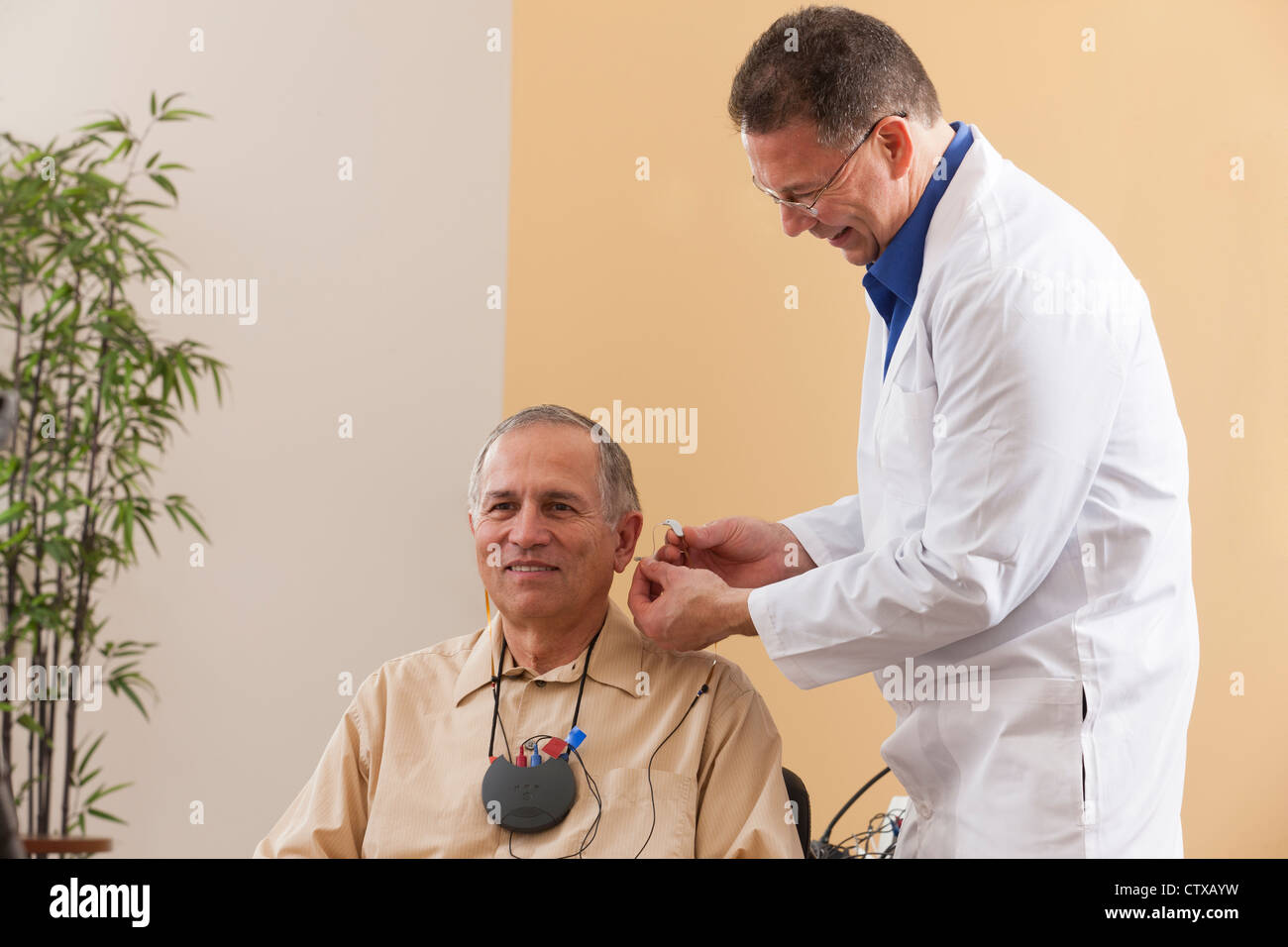 Audiologist inserting behind-the-ear hearing aid into a patient's ear ...