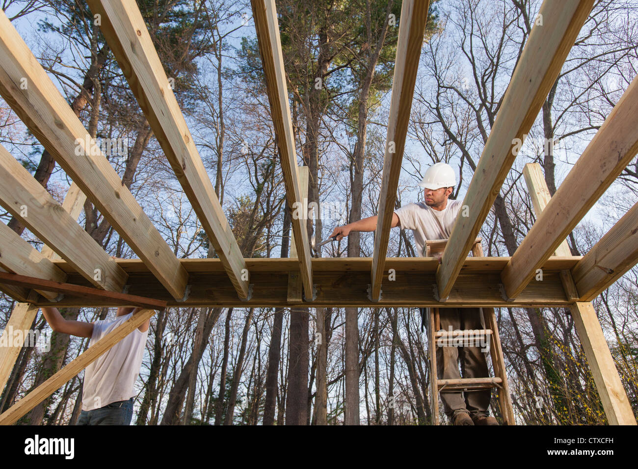 Hispanic carpenter installing first decking with corner cuts around ...