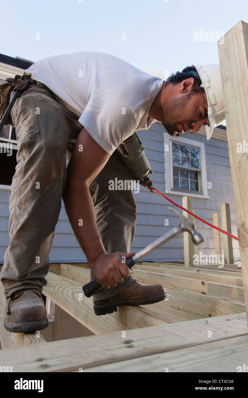 Hispanic carpenter standing on deck joists to hammer nail into decking ...