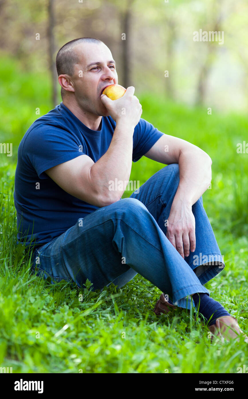 Young man sitting in grass and eating a fresh apple Stock Photo - Alamy