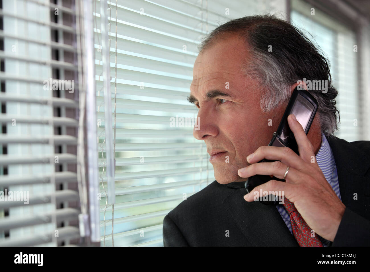 Senior businessman looking through blinds whilst making call Stock ... Senior businessman looking through blinds whilst making call Stock ...
