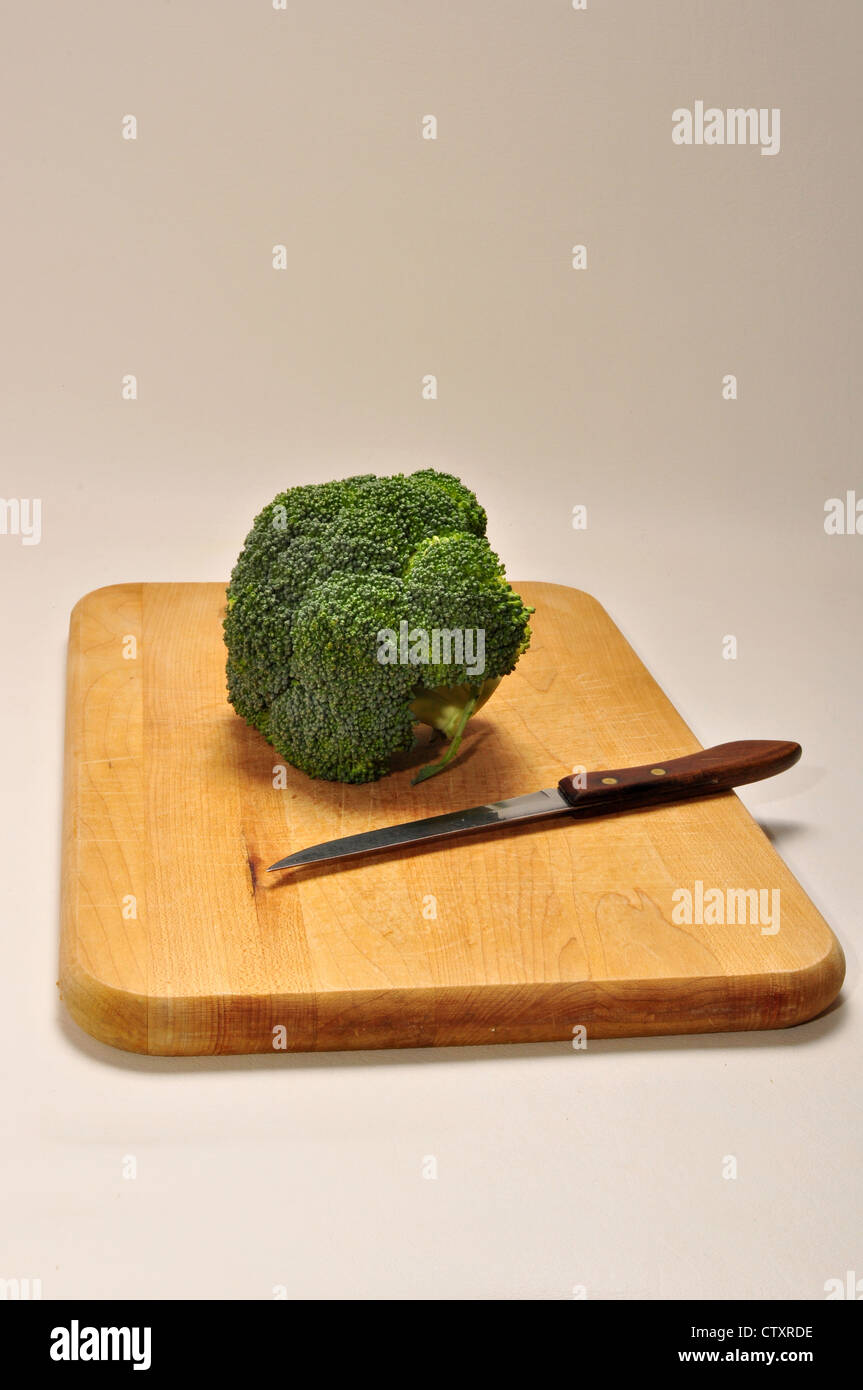 A head of broccoli lays on a wood cutting board with a knife nearby ...