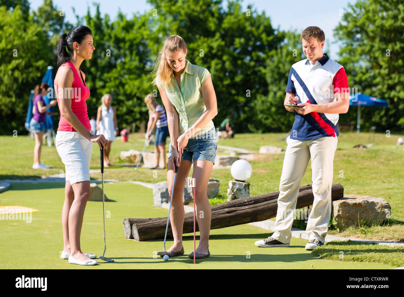 People, man and women, playing miniature golf on a beautiful summer day ...