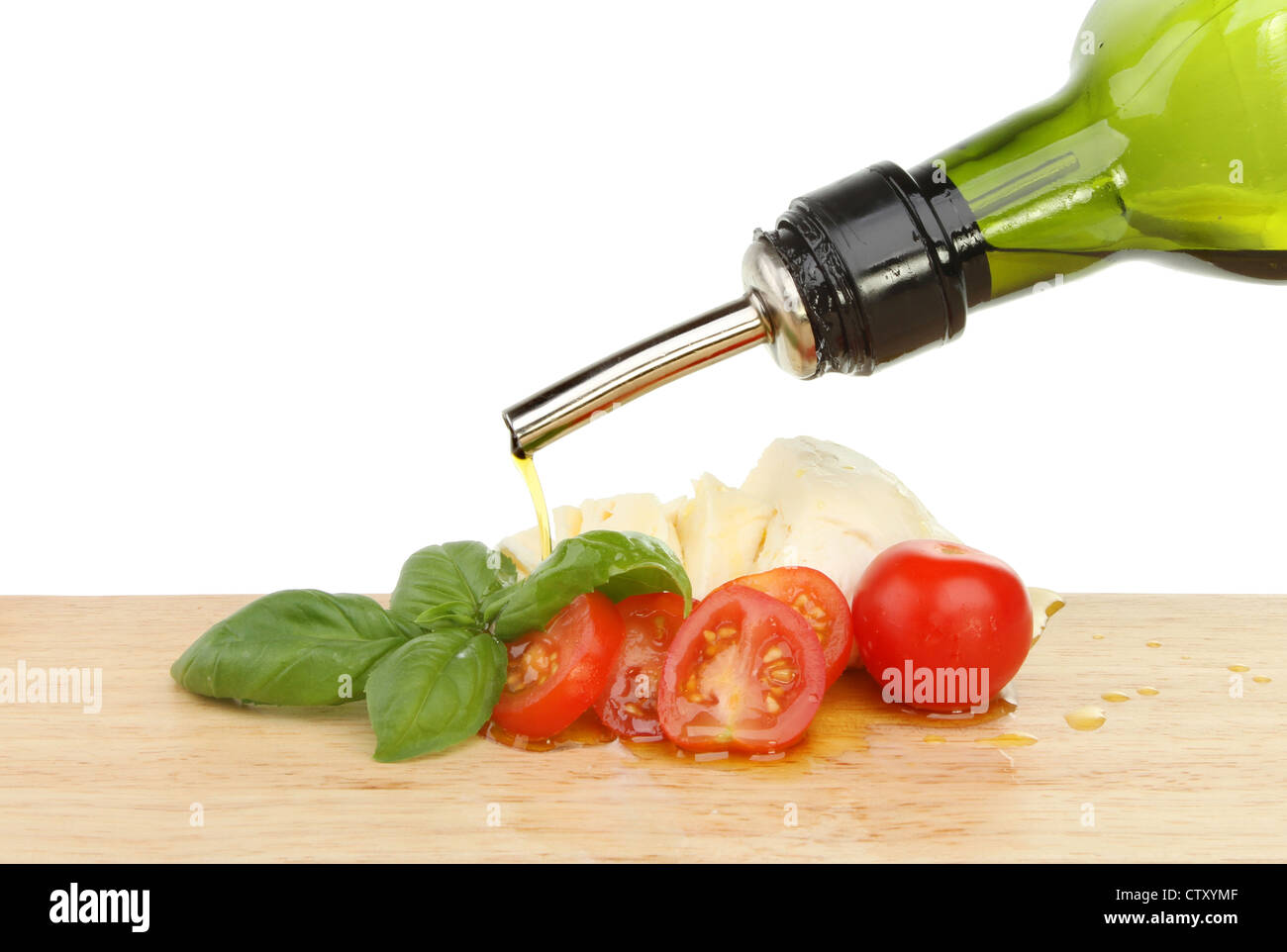 Olive oil pouring over tomato, basil and mozzarella cheese on a wooden ...