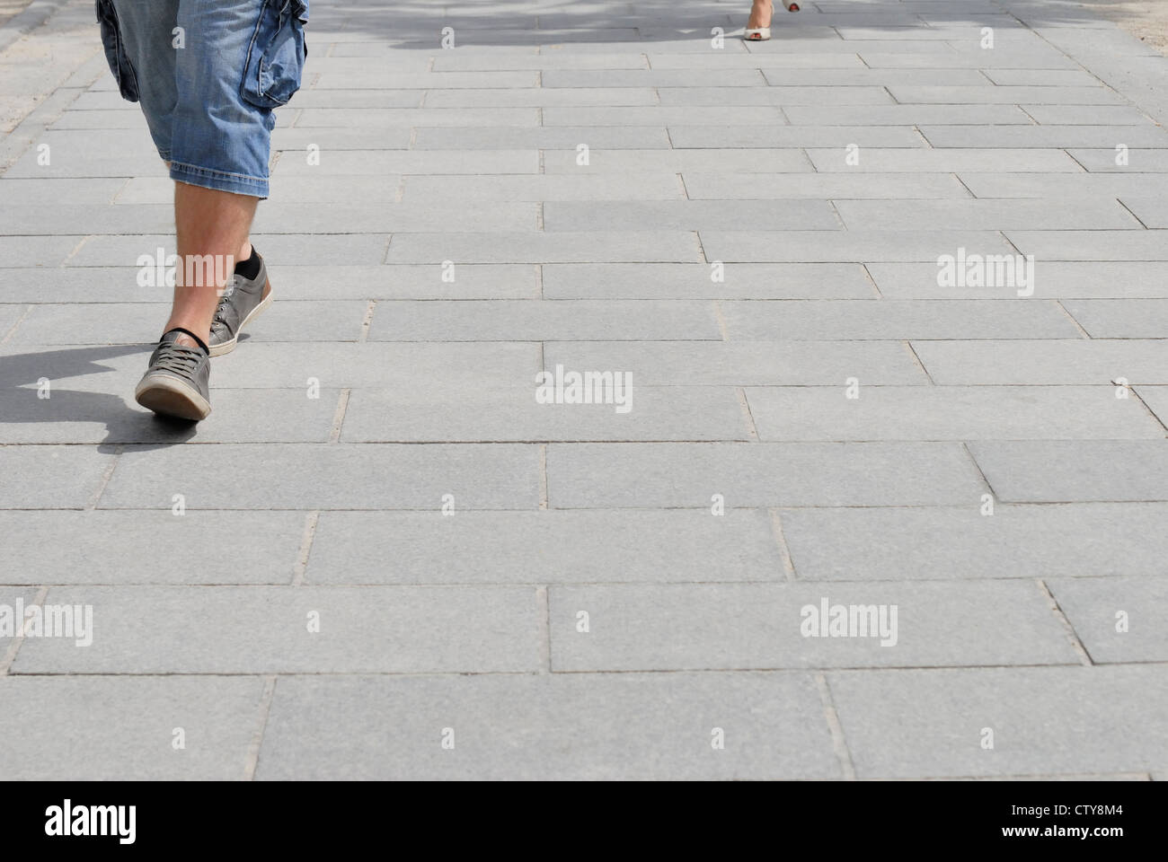 Man's feet walking on pavement - woman behind Stock Photo - Alamy