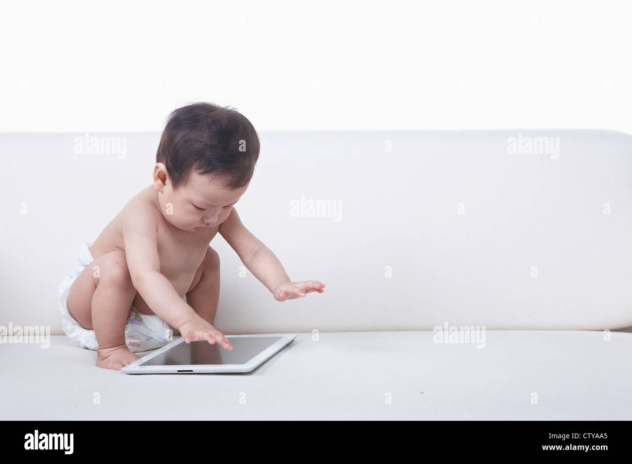 A baby looking at the tablet PC on the couch Stock Photo - Alamy