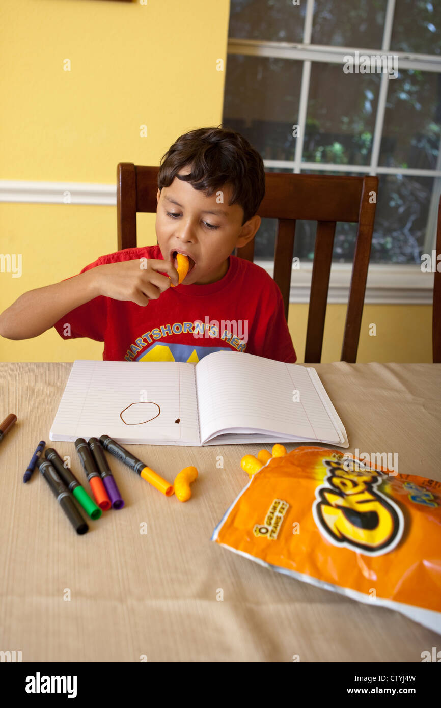 Eight-year-old Mexican-American boy snacks on junk food, Cheetos, while ...