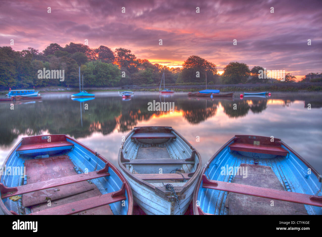 Three rowing boats sit on Rudyard Lake with the purple sky of an early ...