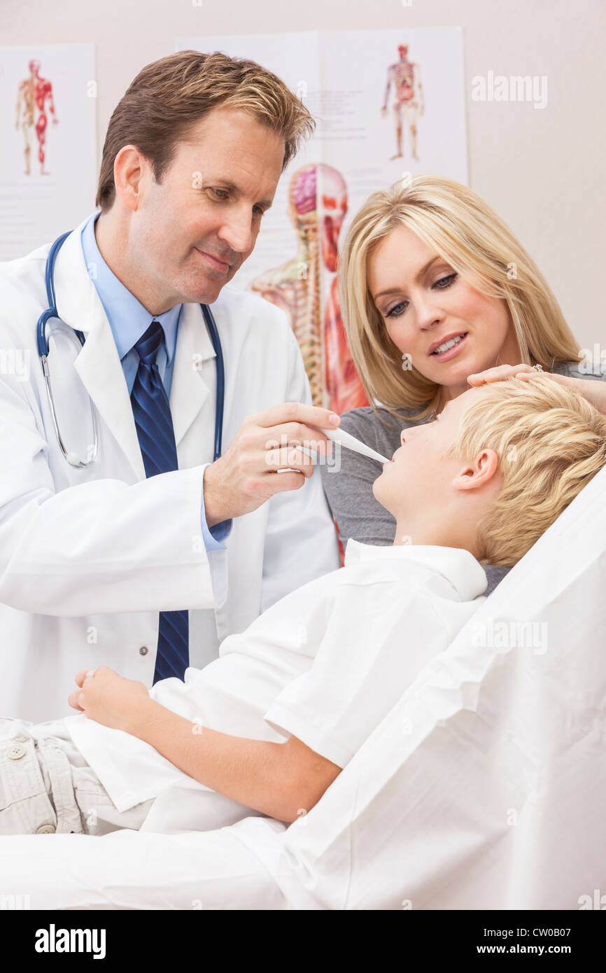 A male doctor examining and taking the temperature of a sick boy child ...