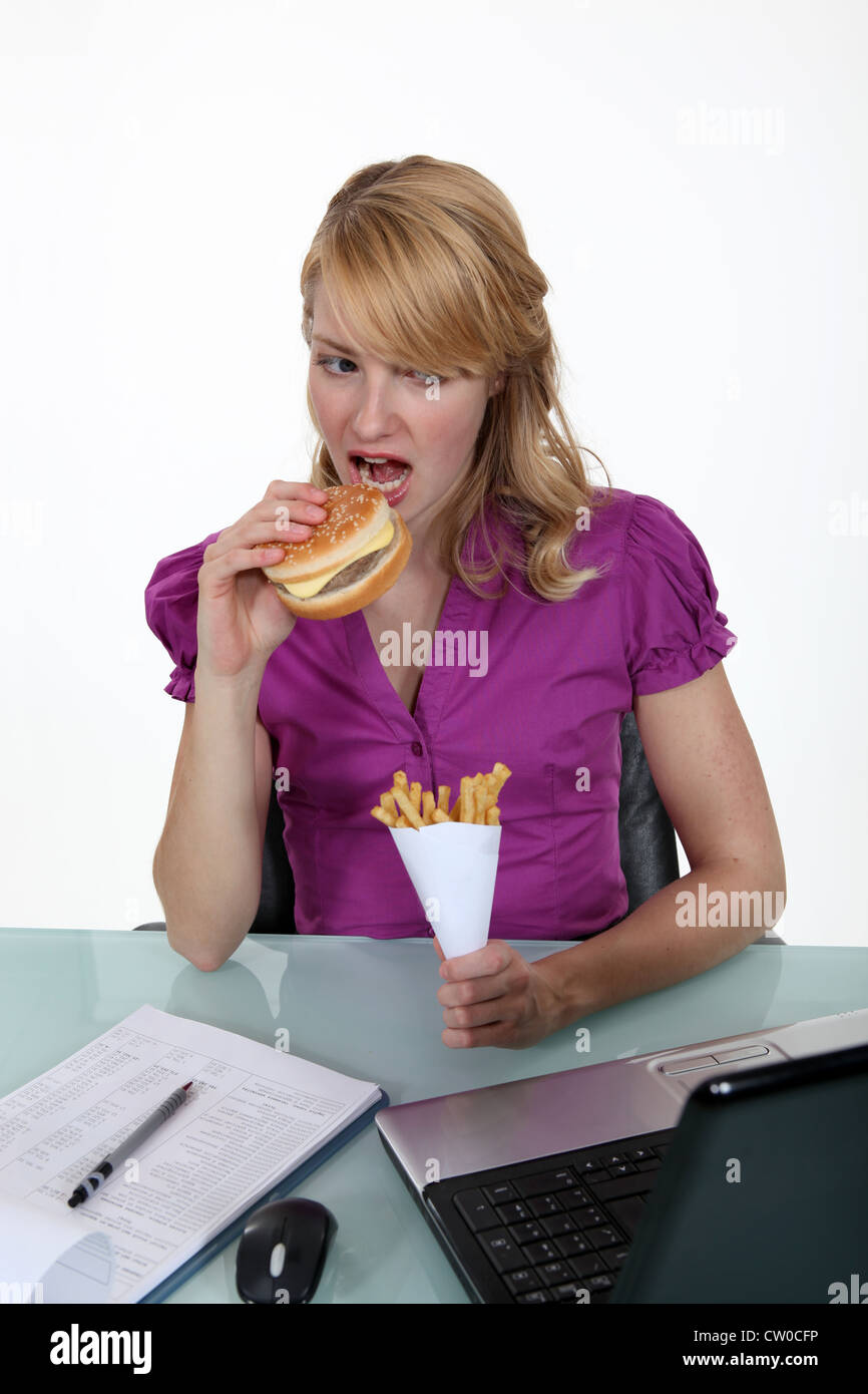 Woman eating junk food at her desk Stock Photo - Alamy