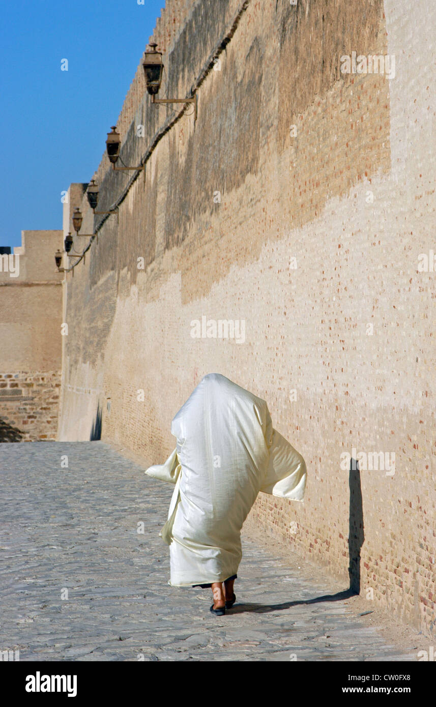 Woman in white chador walks by the walls of the Grand Mosque, Kairouan ...