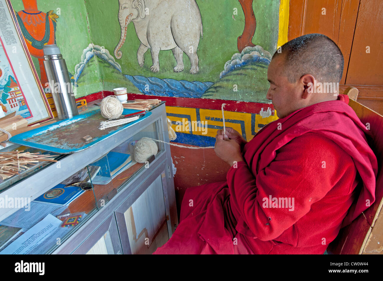 A red-robed Buddhist monk is working at making something out of a ball ...