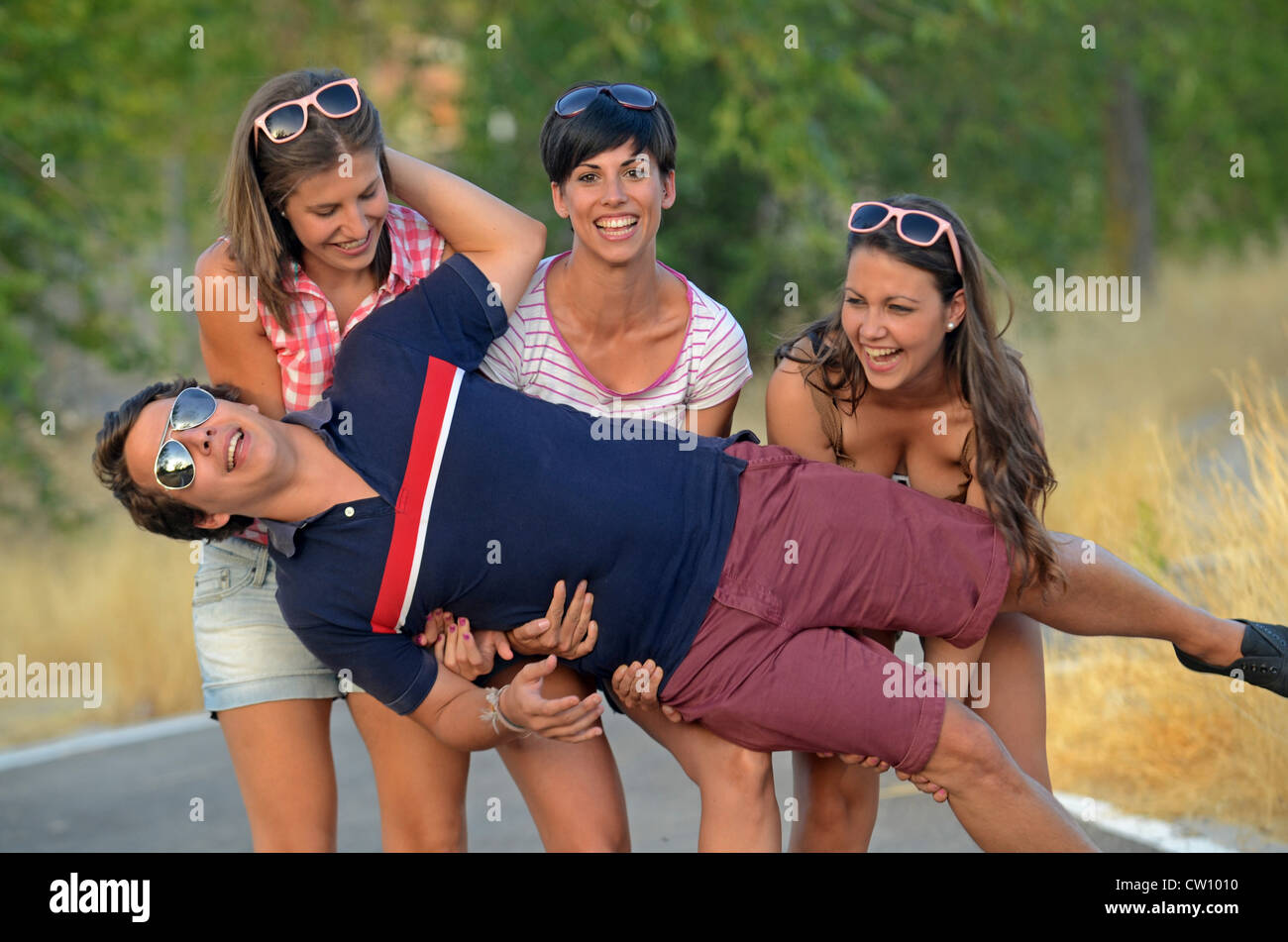 Three young women trying to carry young man on their arms Stock Photo ...