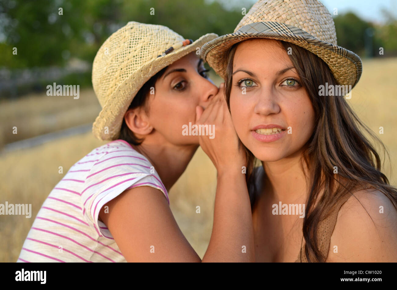 Young woman whispers in friends ear Stock Photo - Alamy