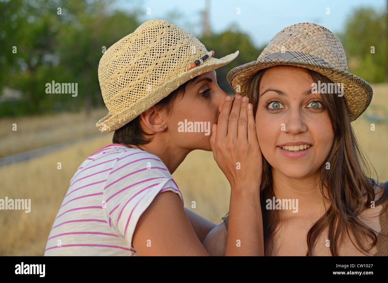 Young woman whispers in friends ear Stock Photo - Alamy