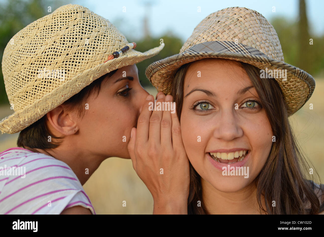 Young woman whispers in friends ear Stock Photo - Alamy
