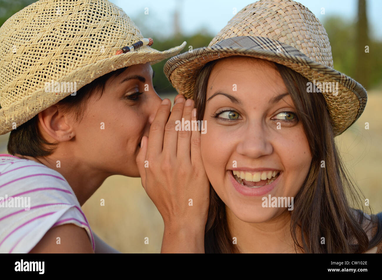 Young woman whispers in friends ear Stock Photo - Alamy