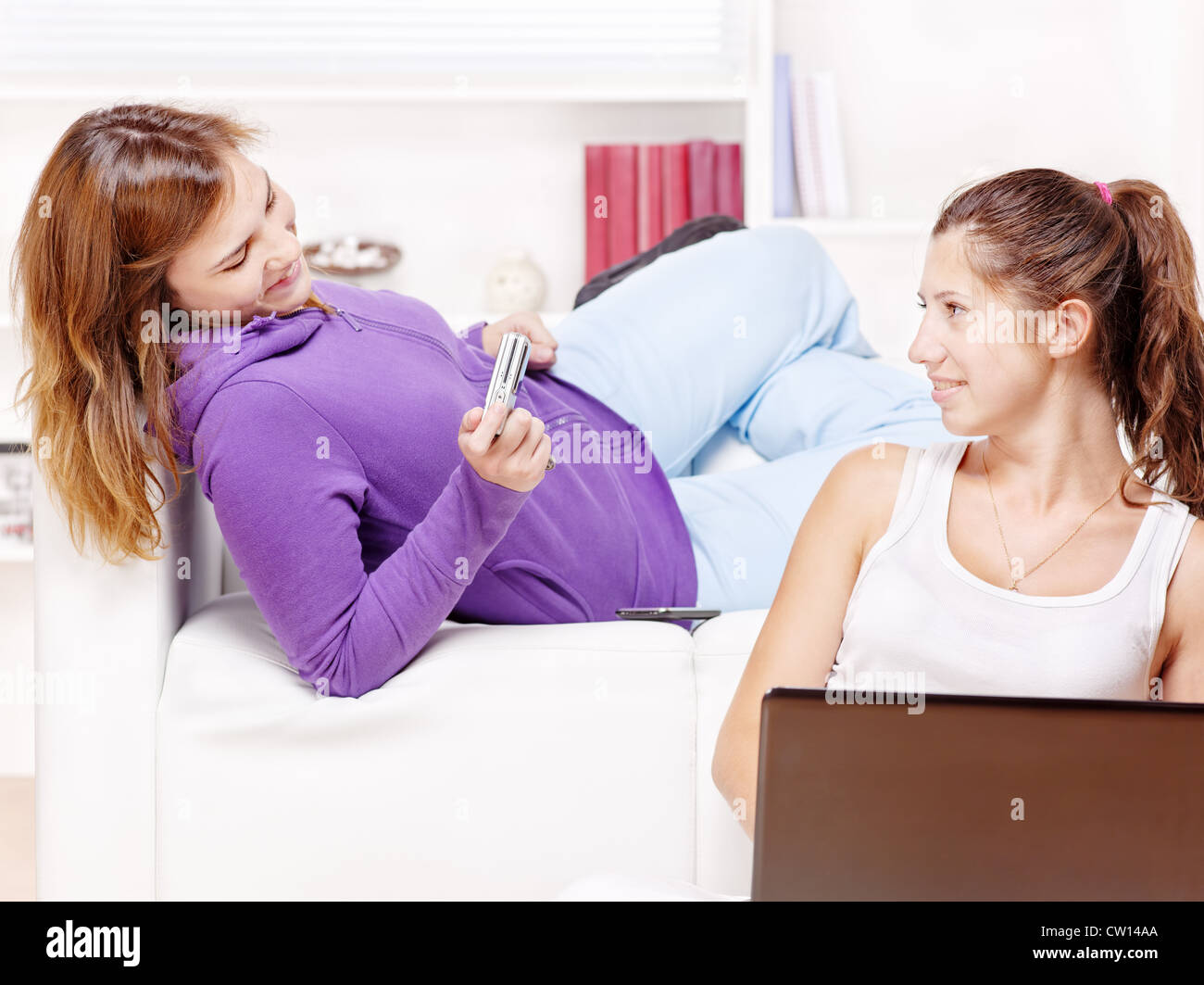 Two happy teenage girls having fun using electronic gadgets at home ...