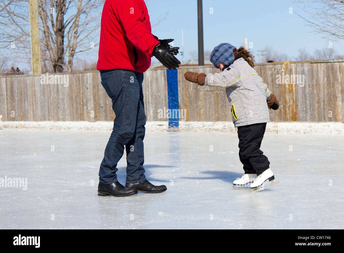 Father teaching daughter how to ice skate at an outdoor skating rink in ...