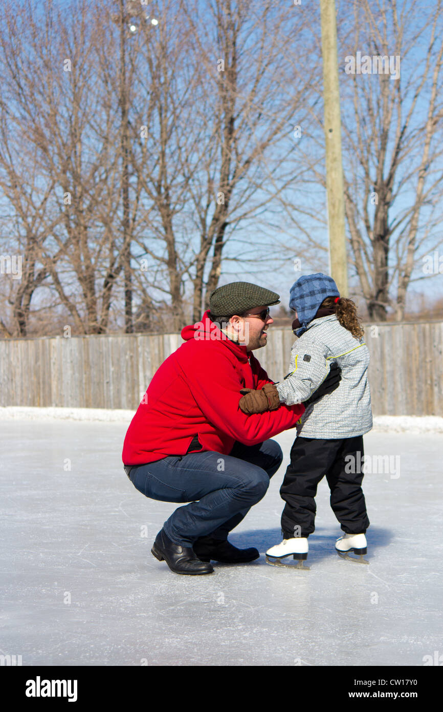 Father teaching daughter how to ice skate at an outdoor skating rink in ...