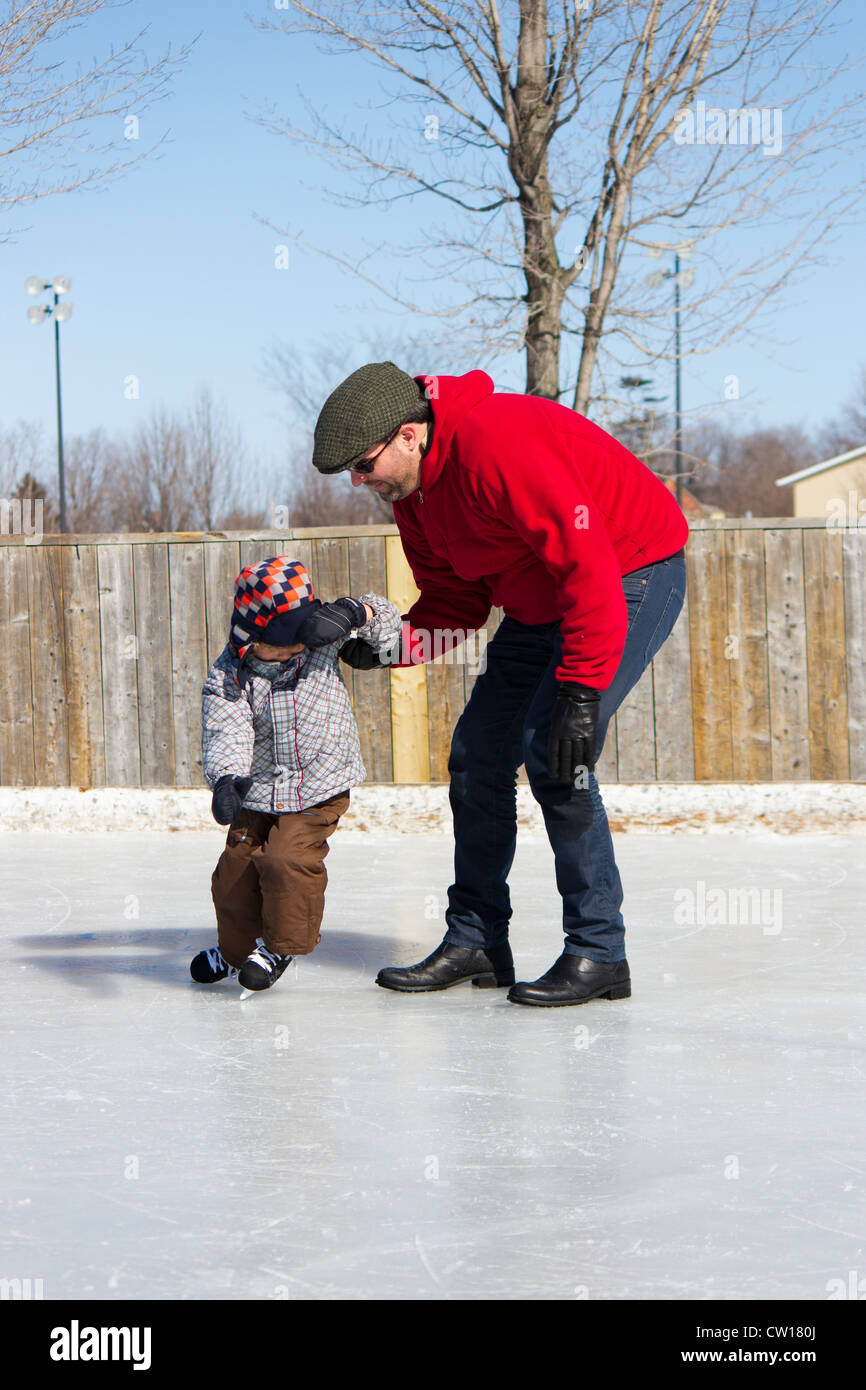 Father teaching son how to ice skate at an outdoor skating rink in ...