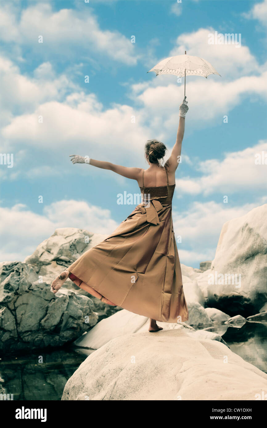 Woman stands on one leg on a rock and balances using an umbrella Stock ...