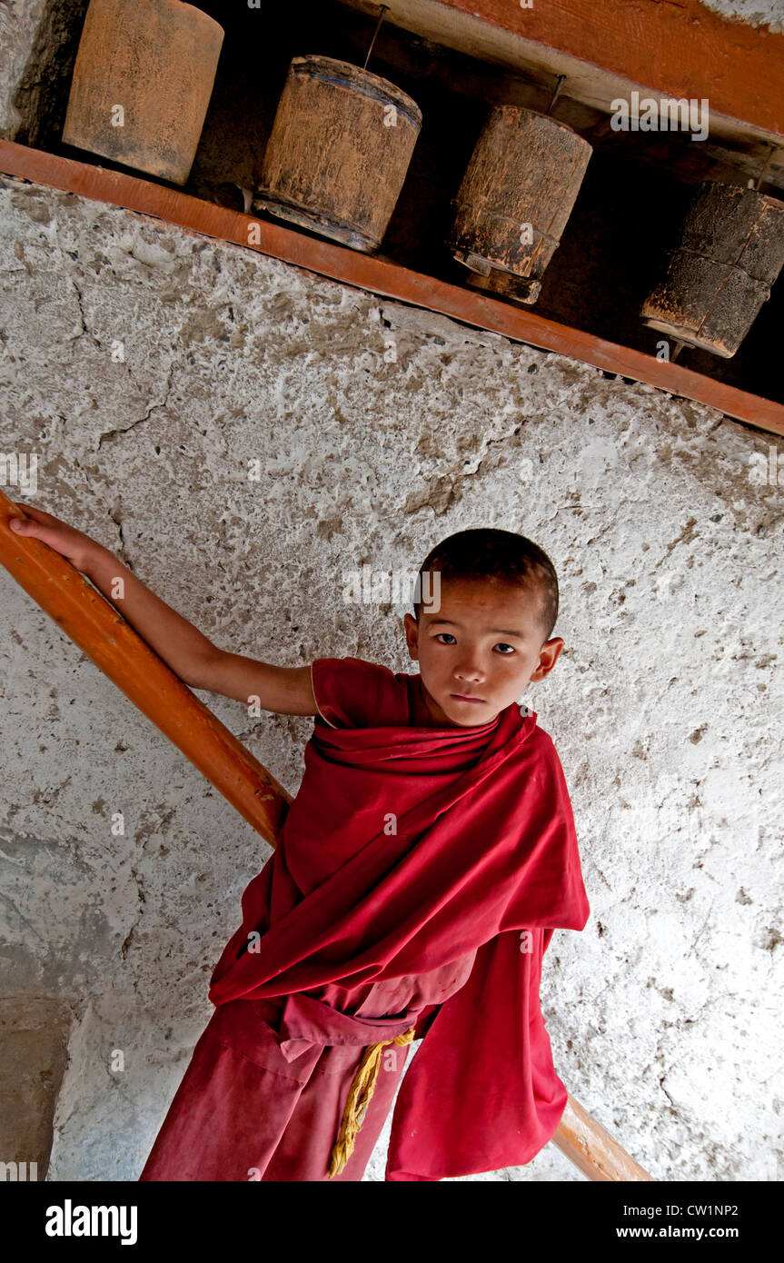A young monk in a red robe against a white stucco wall with prayer ...