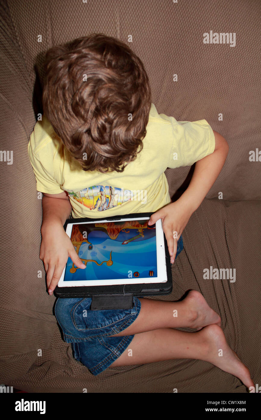 A six year old boy using an iPad tablet computer and playing a game on ...