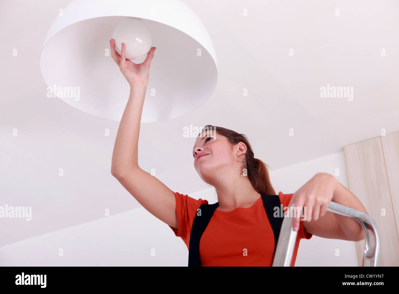 young woman on ladder changing bulb Stock Photo - Alamy