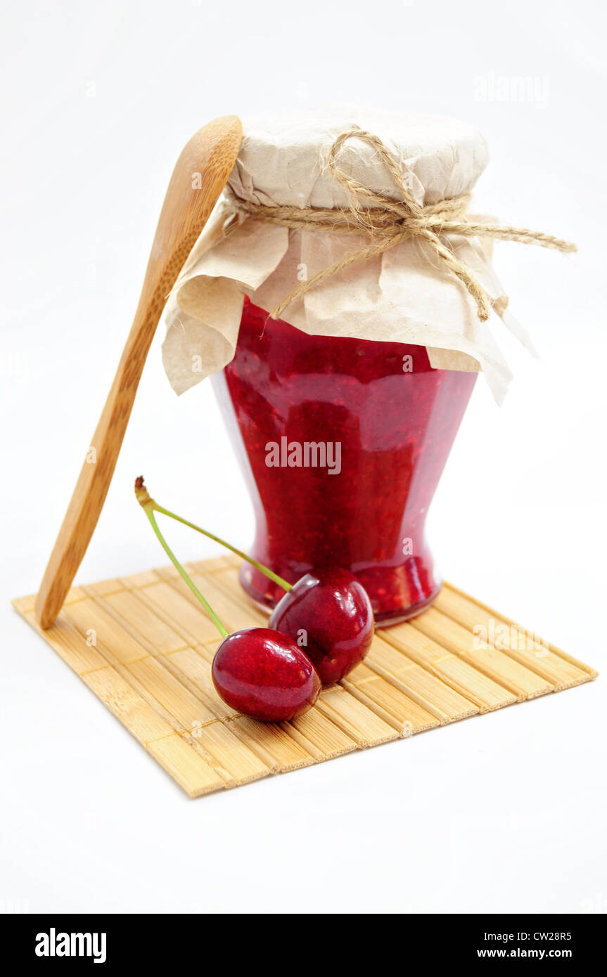 Jar of homemade cherry jam and couple of cherries with wooden spoon and ...