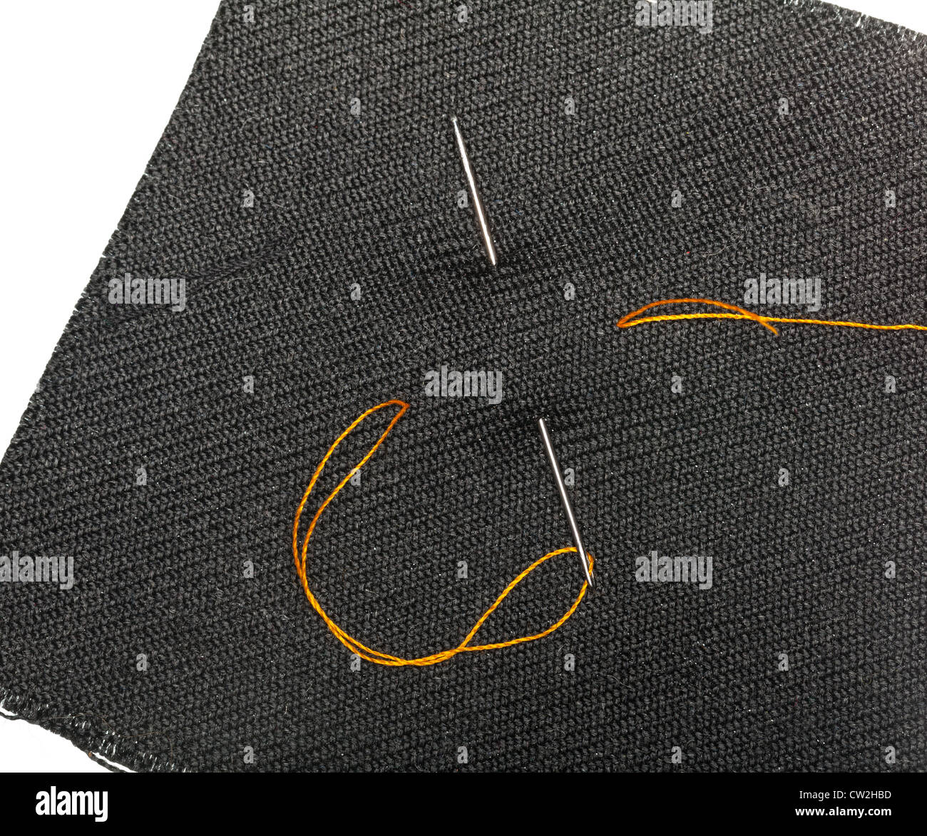 Orange cotton thread and needle pushed through piece of woven black ...