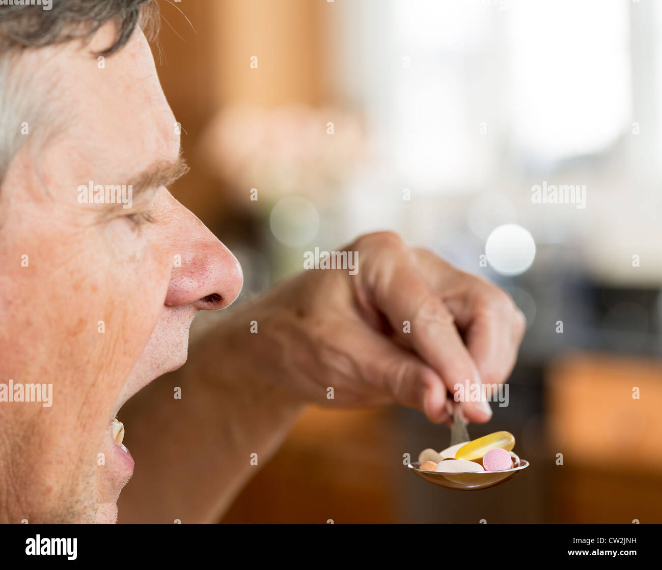 Senior caucasian male eating a spoonful of vitamin tablets for ...