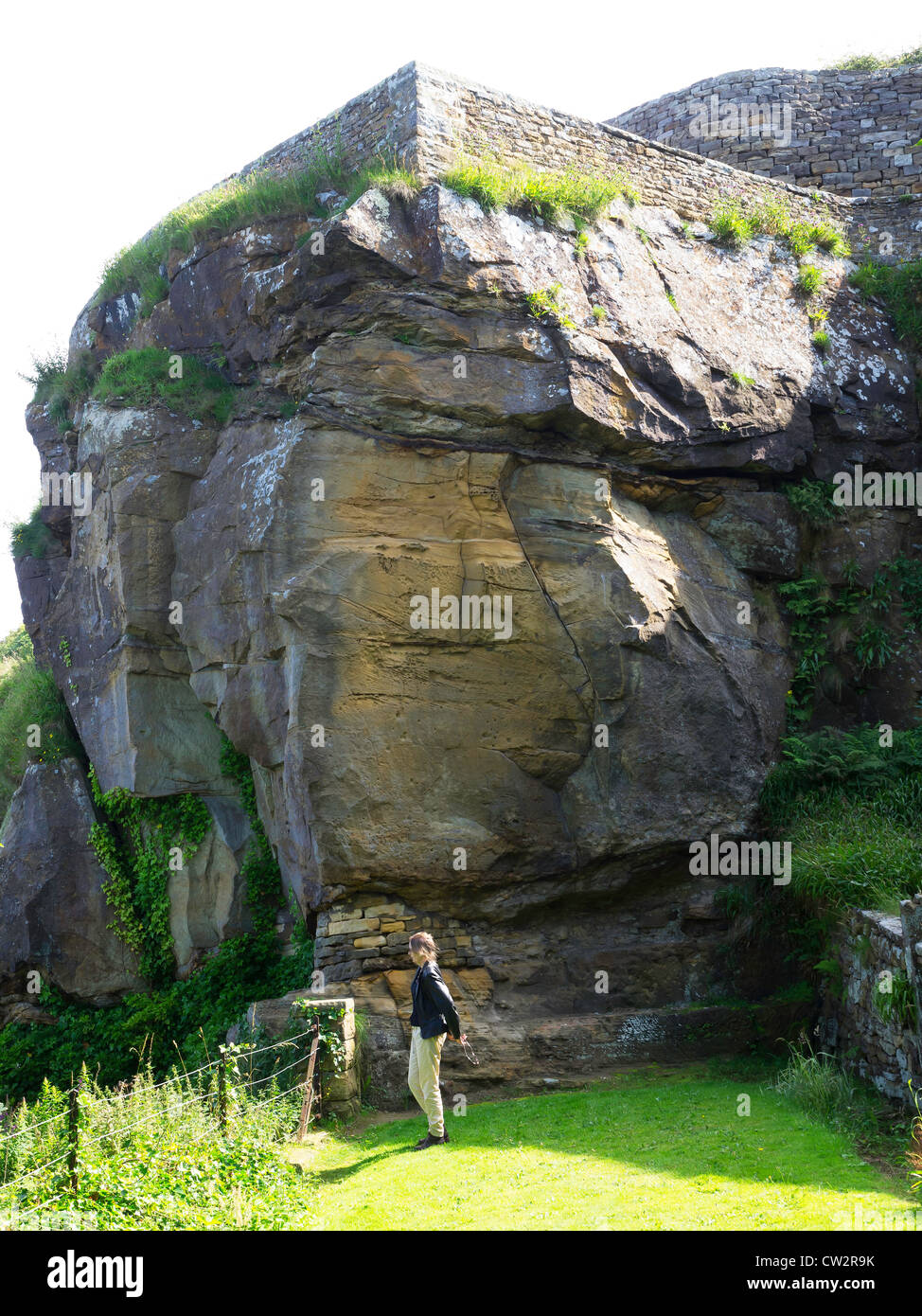 Woman looking out to sea under spectacular sandstone cliff at Ravenscar ...