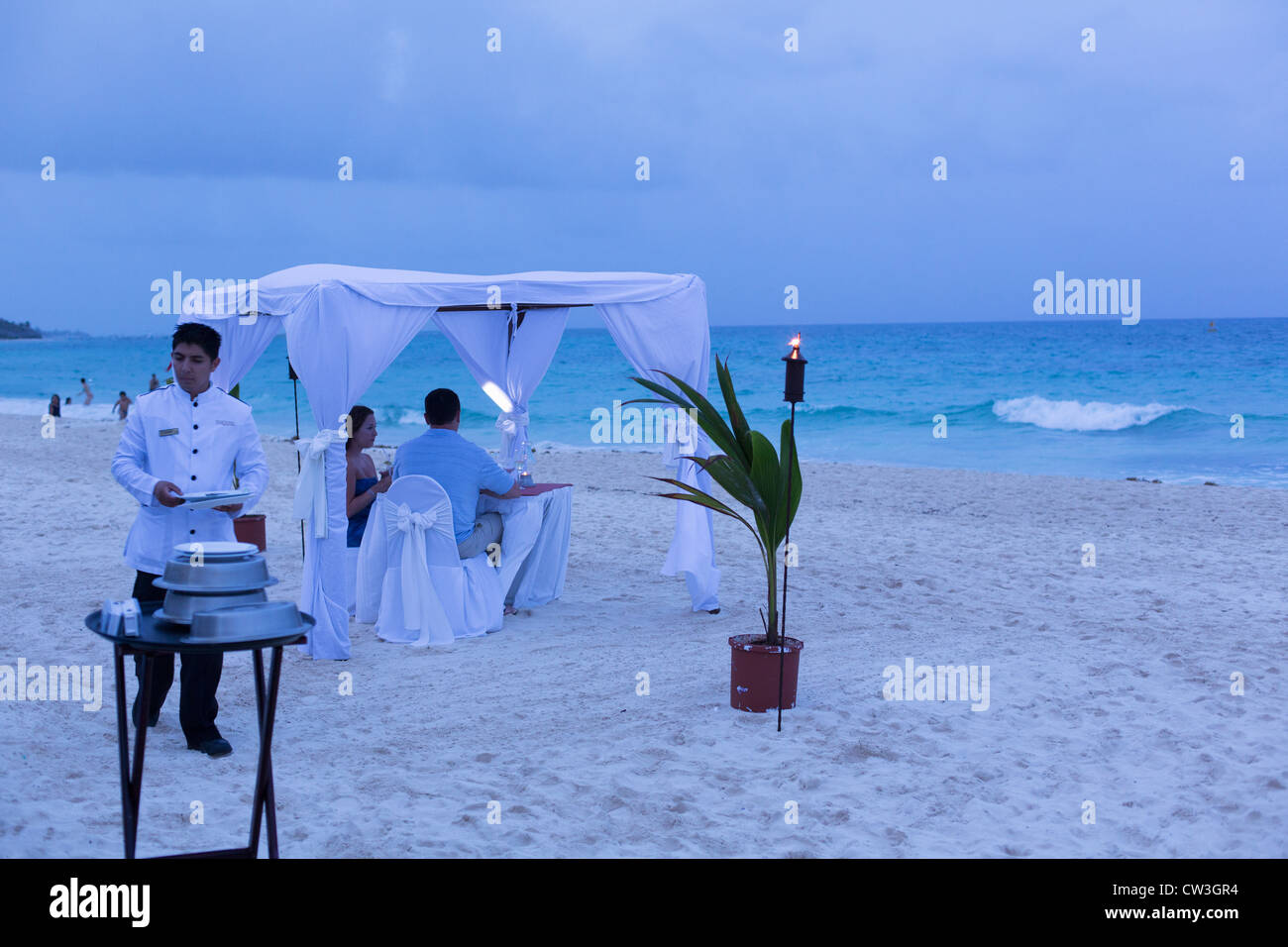 couple having dinner on the beach, under a canopy, being served by a ...