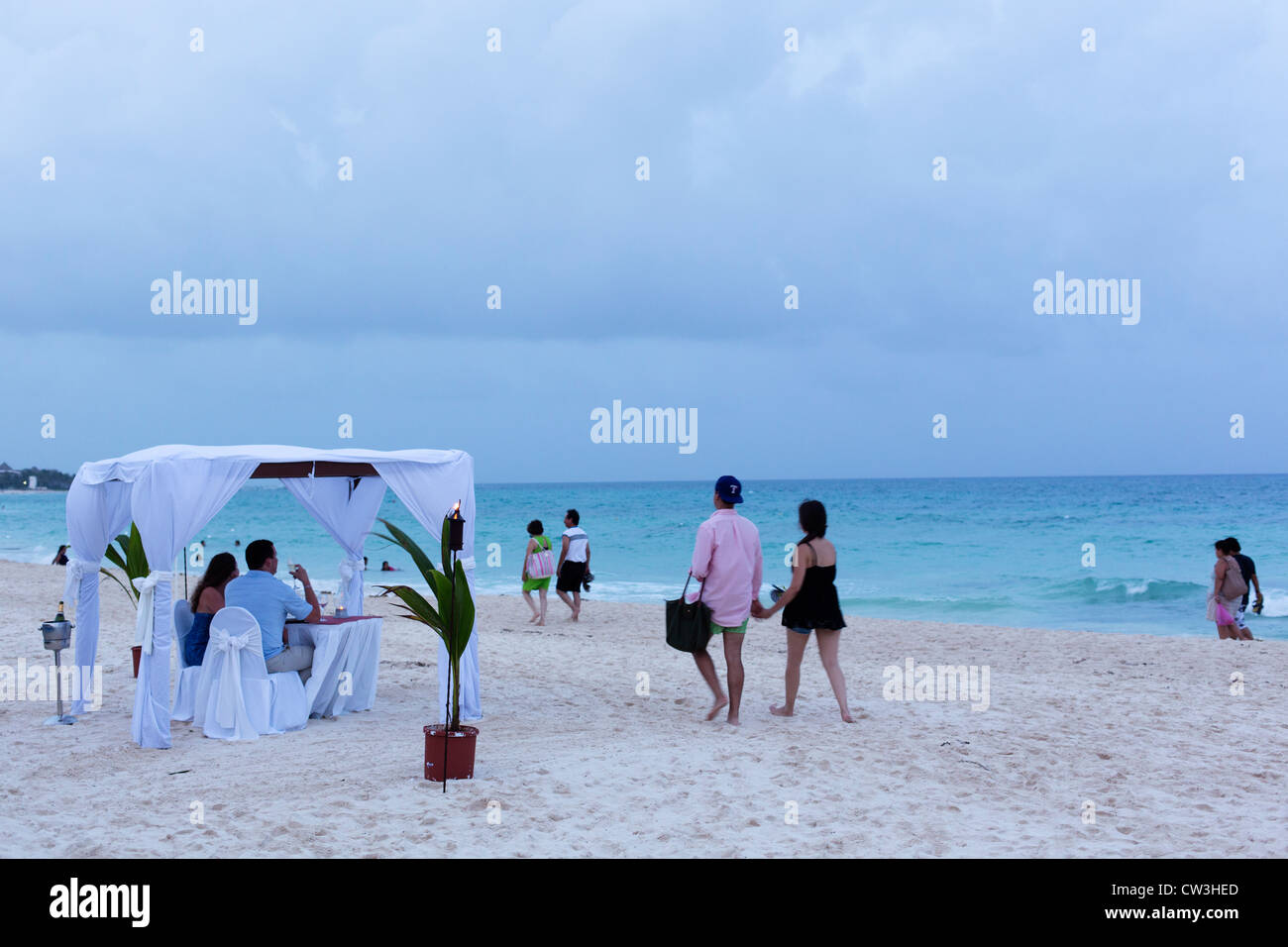 couple having dinner on the beach, under a canopy, being served by a ...