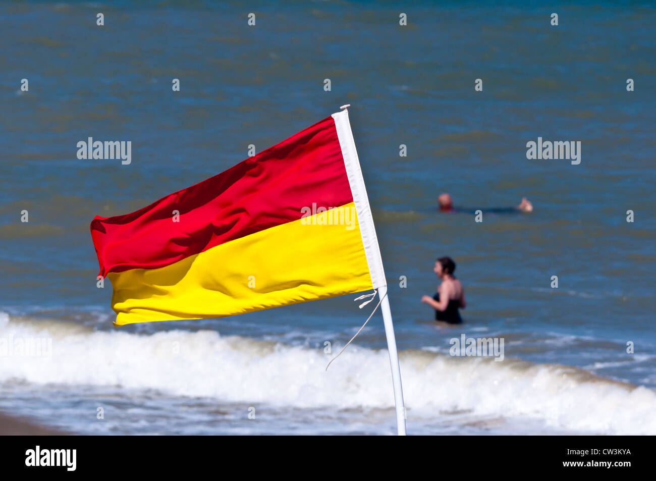 Red and yellow lifeguard flag with swimmers Stock Photo - Alamy
