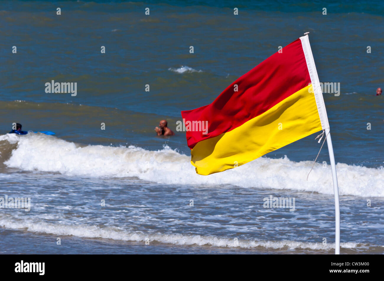 Red and yellow lifeguard flag with swimmers Stock Photo - Alamy