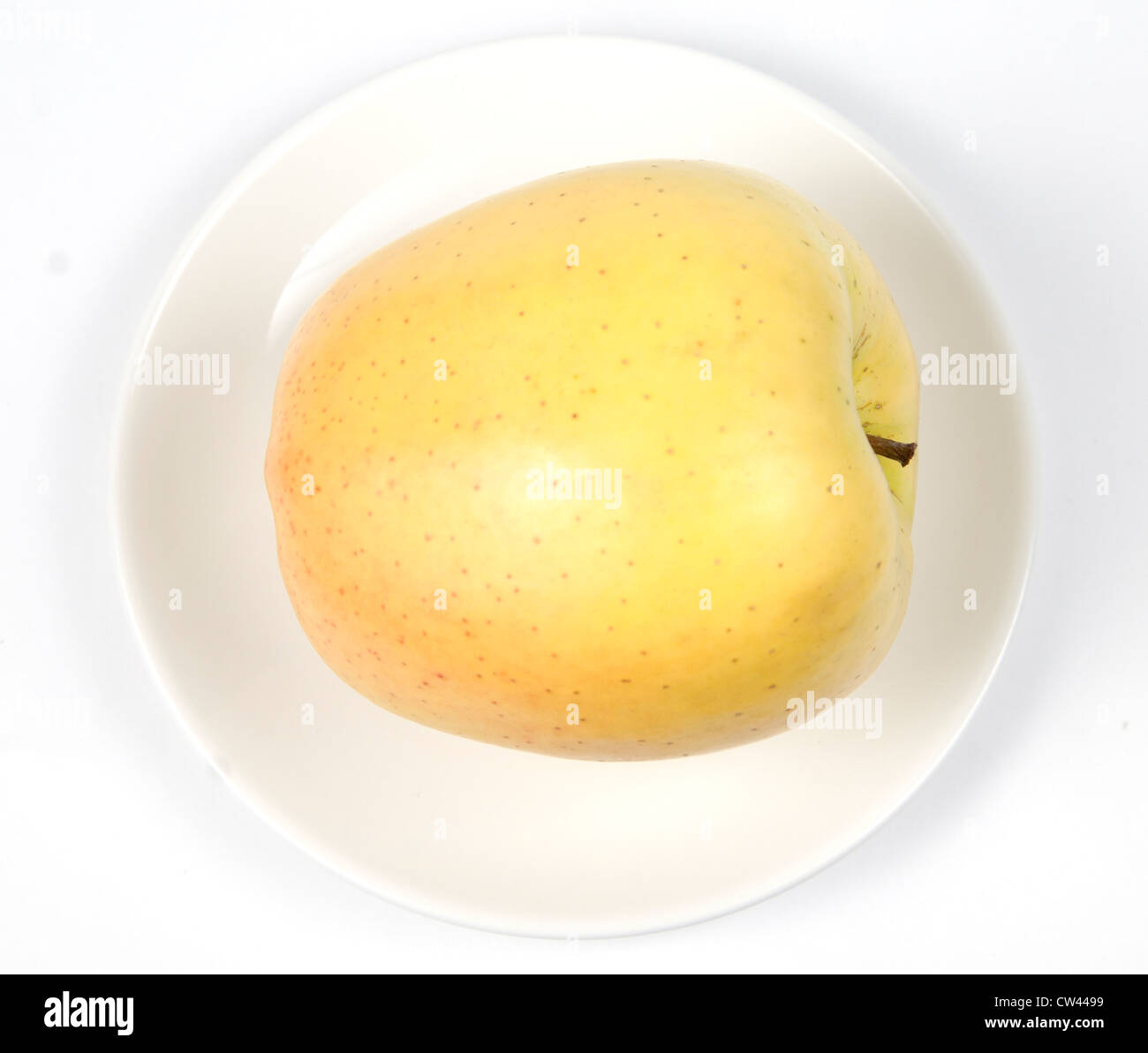 Yellow apple lying on a dish over a light background Stock Photo - Alamy