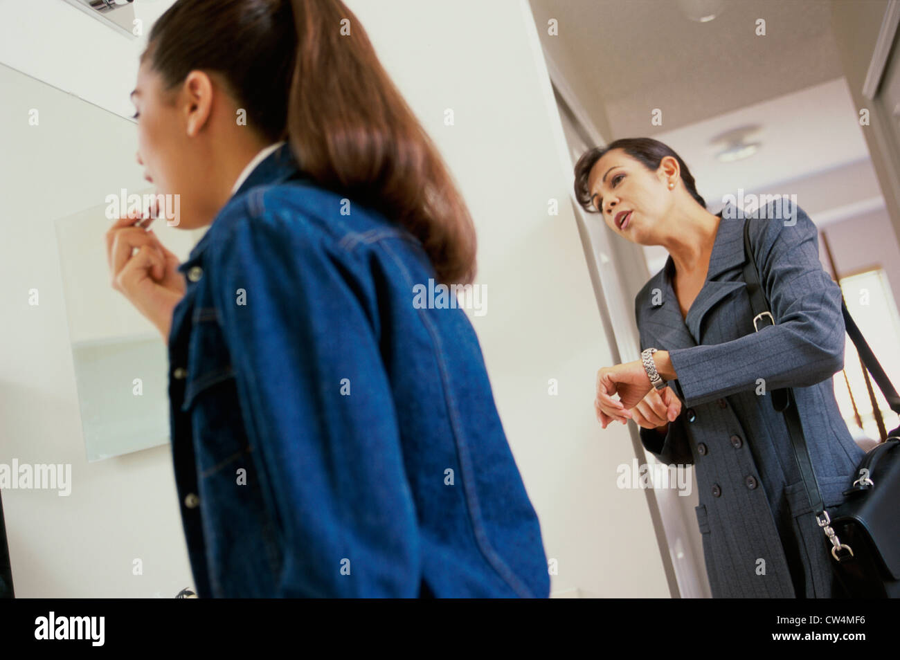 Side profile of a daughter applying lipstick with her mother standing ...